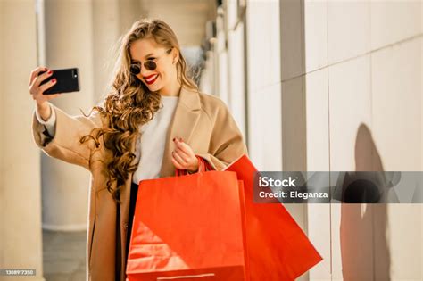 그녀의 휴대 전화로 셀카를 찍고 미소를 지으며 도시에서 쇼핑하는 젊은 여성의 사진 가방에 대한 스톡 사진 및 기타 이미지