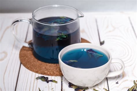 나비 완두콩 블루 꽃 차입니다 건강 한 디 톡 스 허브 드링크 흰 컵에 버터 플라이 완두콩 블루 차와 흰 나무 테이블 흩어져