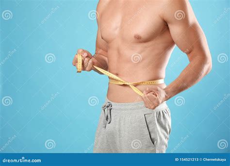 Young Man With Slim Body Using Measuring Tape On Light Blue Background