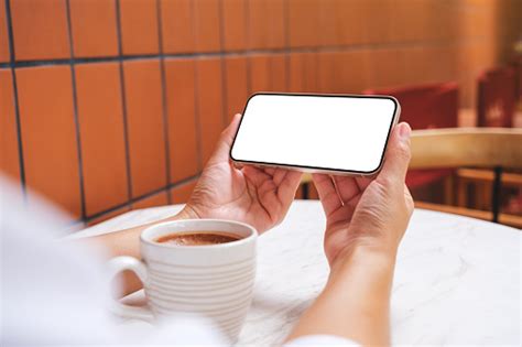 테이블 위에 커피 잔이있는 빈 데스크톱 화면이있는 휴대 전화를 들고있는 여성의 모형 이미지 손에 대한 스톡 사진 및 기타 이미지