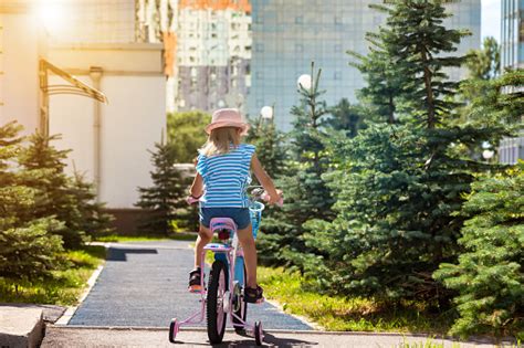 여름 공원 야외에서 자전거를 타는 분홍색 모자를 쓴 어린 아이의 뒷모습 작은 금발 소녀 아이는 화창한 날에 여름철에 밖에서 작은 자전거를 타는 것을 즐깁니다 어린 시절의