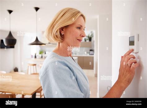 Close Up Of Mature Woman Adjusting Central Heating Temperature At Home On Thermostat Stock Photo
