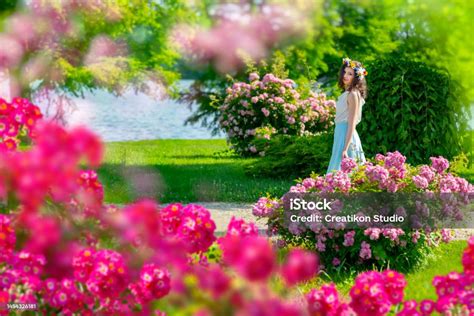 꽃 사이를 걷고 있는 젊은 행복한 미소 판타지 여자의 야외 초상화 젊은 아름다운 여신은 밝은 햇빛 속에서 봄의 자연을 즐깁니다 분홍색 장미 프레임이 있는 동화 이미지 아트