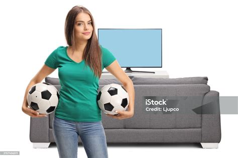 Beautiful Young Woman Holding Two Footballs In Front Of A Sofa And Tv