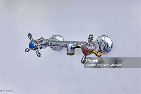 뜨거운 물과 차가운 물을 위한 두 개의 십자형 손잡이가 있는 벽걸이형 금속 수도꼭지 스파우트가 제거되어 나사산 연결이 노출되고 일부 변색되었습니다 0명에 대한 스톡 사진 및