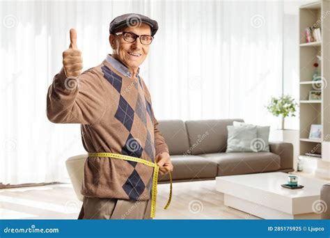 Anciano Midiendo La Cintura Con Una Cinta En Una Sala De Estar Y Haciendo Gestos De Pulgares