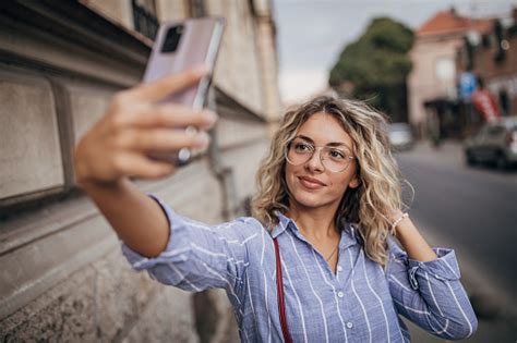 아름다운 여자는 도시 거리에 서서 스마트 폰으로 셀카를 만들기 거리에 대한 스톡 사진 및 기타 이미지 거리 건물 외관 곱슬 머리 Istock
