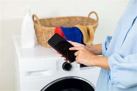 클로즈업 주부 손은 응용 프로그램과 함께 휴대 전화를 사용하여 스마트 세탁기를 작동합니다 기술 스마트 폰으로 제어되는 옷을 청소하는 여성 가사 집안일에 대한 스톡 사진 및