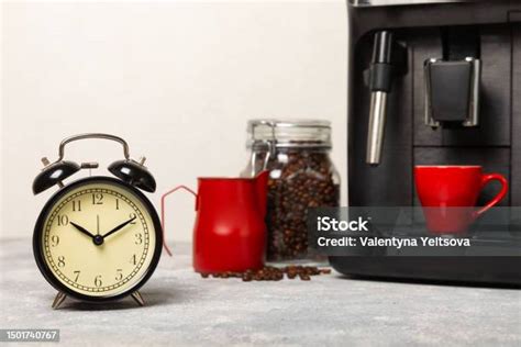 커피 머신의 배경에 알람 시계 아로마 커피 한 잔과 커피 머신을 배경으로 식탁에 놓인 검은색 알람 시계 쾌활한 아침 개념 0명에
