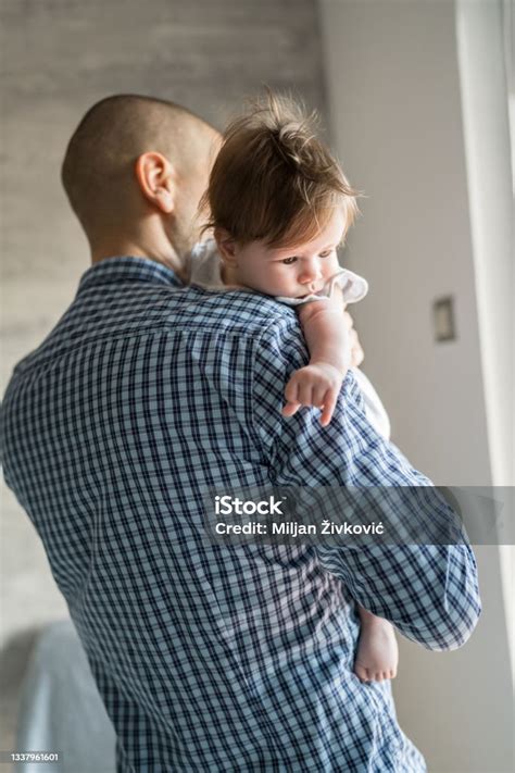 집에서 하루 종일 창문 옆에 서있는 동안 어깨에 아기 딸을 안고있는 아버지의 측면 보기 5 개월 된 소녀 유아가 새로운 삶과 부모 개념 복사 공간을 허비하는 위치에 있습니다