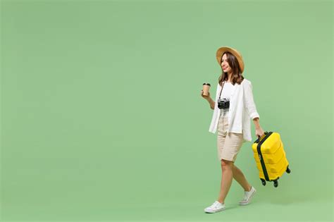 캐주얼 한 옷 모자를 쓴 전체 길이 여행자 관광객 여성은 파스텔 녹색 배경에 고립 된 커피 차 의 종이 컵을 들고 가방을 들고 있습니다 주말 해외 여객 여행 항공 비행 여정