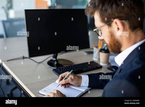 Online Business Class Male Office Worker Writing In Notebook Taking Notes And Using Computer