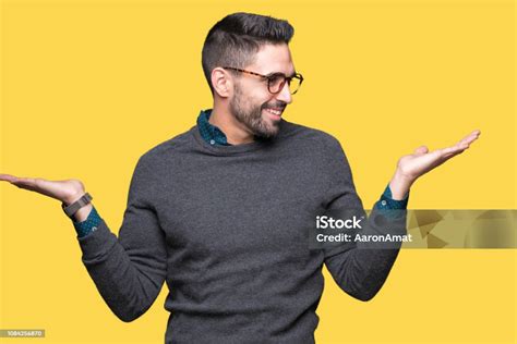 젊은 잘생긴 남자에 안경을 절연 배경 미소 보여주는 두 손 열 손바닥 제시 하 고 광고 비교 및 균형 비교에 대한 스톡 사진 및 기타 이미지 Istock