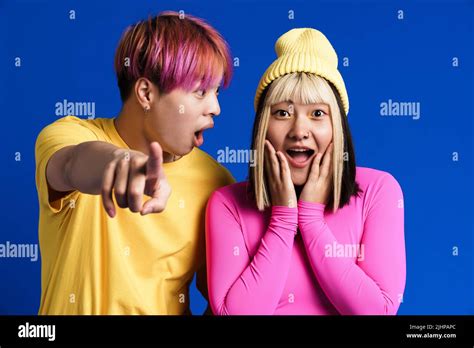Asian Teenagers Pointing Finger At Camera While Expressing Surprise Isolated Over Blue Wall