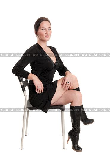 Молодая брюнетка в черном платье и сапогах сидит на стуле Стоковое фото № 5536010 фотограф
