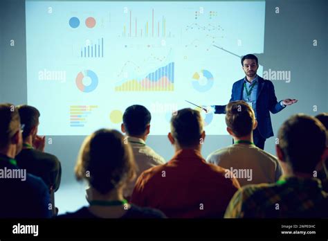 Businessman Speaker Delivering Presentation To Attentive Crowd With
