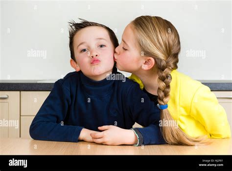 Jolie jeune fille donne à son petit frère pour un baiser à la maison dans la cuisine Photo Stock