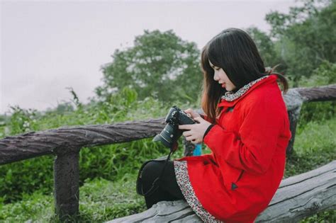 Premium Photo Side View Of Woman Holding Camera While Sitting On Log
