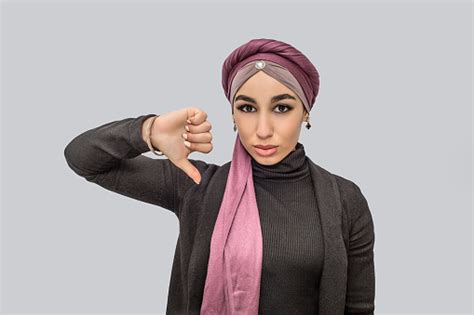 젊은 아라비아 여자 스탠드 및 Hlold 큰 Thumb 다운입니다 그녀는 카메라에 보인다 모델은 심각한 그녀는 Hidjab와 검은 드레스를 착용 회색 배경에 고립 검은색에