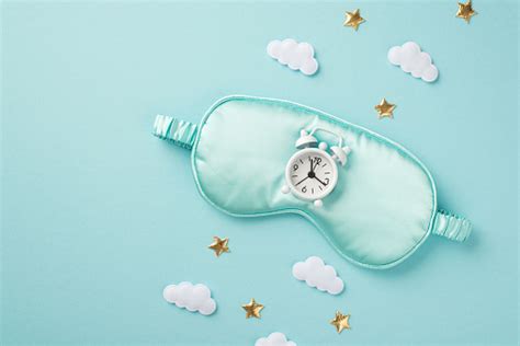 빈 공간이있는 고립 된 파스텔 블루 배경에 파란색 실크 수면 마스크 구름과 황금 별에 흰색 알람 시계의 상단 보기 사진 개념에