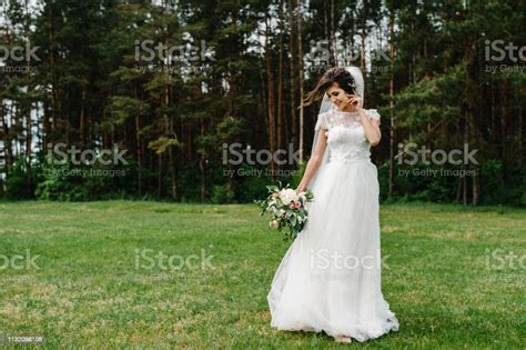 우아한 드레스에 젊은 아름 다운 신부는 자연에서 리본으로 분홍색 꽃과 녹색의 꽃다발을 들고 숲 근처 필드에 서 있다 야외 결혼식 후 복고풍에 대한 스톡 사진 및 기타 이미지