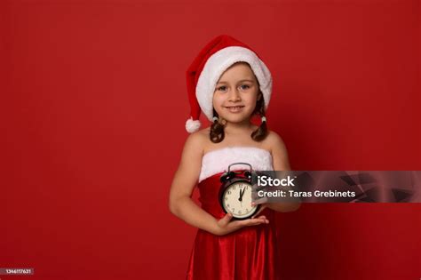 크리스마스와 새해 개념 아름다운 작은 아이 산타 의상에 귀여운 아기 소녀는 얼굴 시계에 자정알람 시계를 들고 광고를위한 공간이있는 빨간색 배경에 대한 카메라를보고 4 5세에