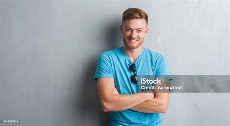 교차 팔 카메라 보고 웃 고 캐주얼 의상 행복 한 얼굴을 입고 회색 그런 지 벽에 빨강 머리 젊은 남자 긍정적인 사람입니다