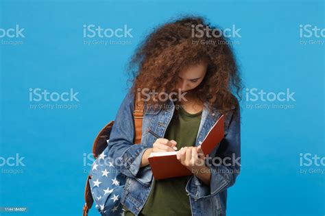 데님 옷에 젊은 아프리카계 미국인 소녀 사춘기 학생 배낭은 파란색 벽 배경 스튜디오 초상화에 고립 된 책을 잡아 고등학교 대학