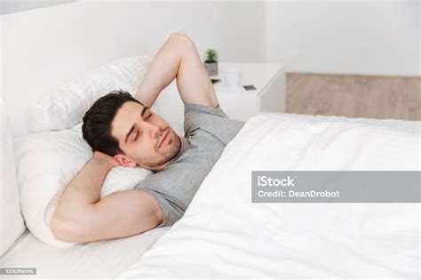 캐주얼 티셔츠를 입은 졸린 면도되지 않은 남자의 초상화 집에서 혼자 낮잠을 자고 있는 흰색 깨끗한 린넨이 머리 밑에 손을 얹고 T 셔츠에 대한 스톡 사진 및 기타 이미지