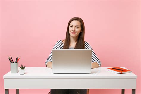 캐주얼 옷 프로젝트 작업을 노트북으로 사무실에 앉아 파스텔 핑크 배경에 고립 동안에 젊은 성공적인 여자 성과 비즈니스 경력 개념입니다 광고에 대 한 공간을 복사 합니다 갈색