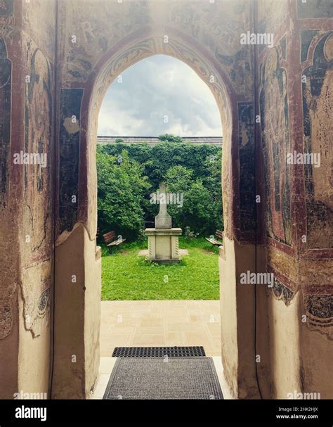 Portrait Of An Arch Passageway Leading Outside To A Concrete Cross In The Middle Of Benches