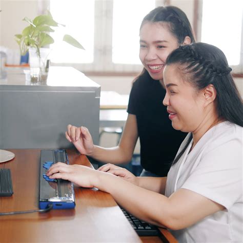 Women Smiling At A Computer While One Uses A Refreshable Braille Display