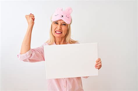 고립된 흰색 배경 위에 배너를 들고 수면 마스크 잠옷을 입은 중년 여성은 분노로 짜증나고 좌절하고 미친 듯이 고함을 지르며 분노 개념 감정에 대한 스톡 사진 및 기타 이미지