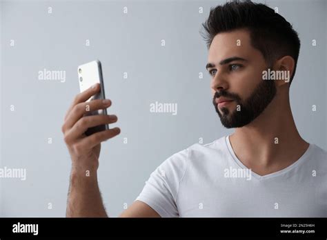 Young Man Unlocking Smartphone With Facial Scanner On Grey Background Biometric Verification