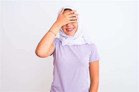고립 된 흰색 배경 위에 서있는 히잡을 입은 젊은 아름다운 아라비아 소녀는 놀라움을 위해 눈을 가리는 얼굴에 손으로 웃고 있습니다 블라인드 개념 가리기에 대한 스톡 사진 및