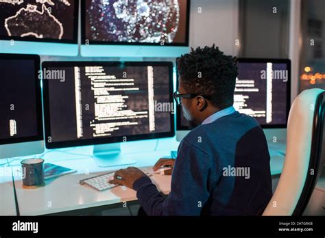 Young African Male Software Developer Working Late In Front Of Computer Screen With Coded Data