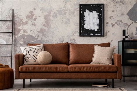 모의 포스터 프레임 현대적인 갈색 소파 베이지색 베개 검은색 화장실 및 세련된 개인 액세서리가 있는 로프트 산업 아파트의 인테리어 디자인 콘크리트 회색 벽입니다 가정 장식