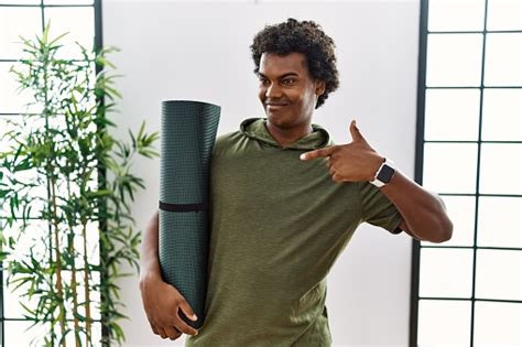 스튜디오에서 요가 매트를 들고 곱슬 머리를 가진 아프리카 남자는 얼굴에 미소를 지으며 자신감을 보이며 자랑스럽고 행복한 손가락으로 자신을 가리킵니다 가리키기에 대한 스톡