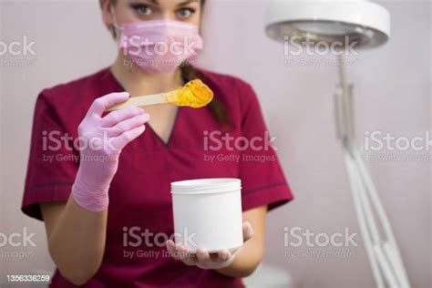 미용사는 항아리에서 설탕 페이스트를 취합니다 으르렁거리고 주걱으로 용기밖으로 설탕 페이스트 설탕 을 위한 설탕 페이스트 미용실에서 설탕을 섭취 개념에 대한 스톡 사진 및