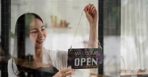 앞치마를 두른 젊은 바리스타 소녀가 카페에 서서 열린 간판을 들고 웃고 있는 초상화 우아한 아시아 커피 숍 여성 직원은 아침에