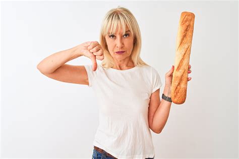 화가 얼굴 엄지 손가락으로 싫어하는 것을 보여주는 부정적인 기호 거부 개념으로 고립 된 흰색 배경 위에 서있는 빵을 들고 있는 중년 제빵사 여성 개념에 대한 스톡 사진 및