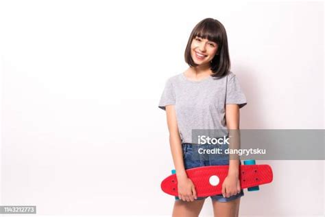 서 있고 흰색 배경 위에 고립 된 카메라를 보고 있는 동안 스케이트 보드와 함께 포즈 선글라스에 예쁜 젊은 여자의 전체 길이 초상화 명랑한에 대한 스톡 사진 및 기타 이미지