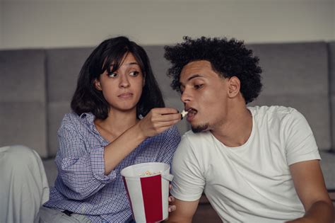 집에서 소파 근처 바닥에 앉아서 팝콘을 먹는 동안 옆으로 보고 웃는 커플의 이미지 2명에 대한 스톡 사진 및 기타 이미지 2