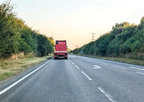 A Large Red Flatbed Lorry Seen From Behind As It Travels Along The Road