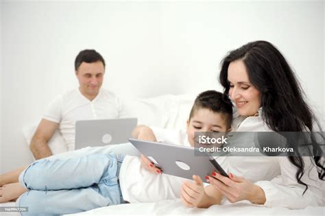 최신 기술 가제트 태블릿에서 노는 엄마와 아들 하얀 침대에 앉아 노트북 원격 작업 프리랜서 휴가 가족 결합 일과 함께 가족과 함께 시간 보내기 3 명에 대한 스톡 사진 및