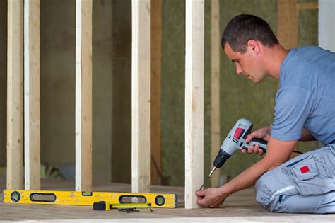 다락방의 내부는 재건에서 오크 바닥으로 절연 된 방 젊은 직업 노동자는 미래 벽을 위한 나무 프레임을 설치 하는 수준과 스크루 드라이버를 사용 합니다 리노베이션 및 개선