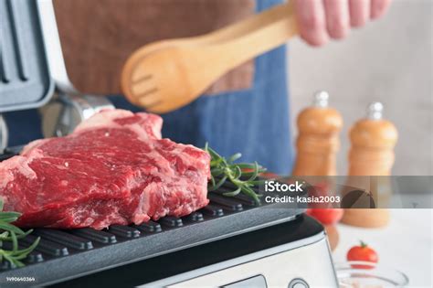 전기 그릴에 생 프라임 스테이크 로즈마리 방울 토마토 후추를 곁들인 현대적인 전기 그릴에 스테이크 립아이를 들고 있는 셰프 남성 현대 부엌에서 요리 과정입니다 평면도 복사