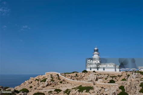 바위가 많은 절벽 꼭대기에 하얀 등대가 있고 흰색 벽이 있고 배경에 바다가 있고 카발레리아 케이프 등대 포넬스 메노르카 스페인 0명에 대한 스톡 사진 및 기타 이미지