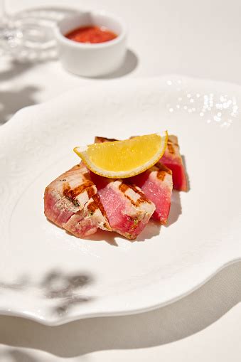 그림자가있는 밝은 배경에 구운 참치 스테이크 흰 테이블에 레몬을 곁들인 구운 참치 구운 생선 스테이크와 미적 구성 바베큐 참치 스테이크 생선 구이 여름 메뉴