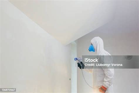 공기없는 스프레이 페인트 작업자는 흰색으로 공기가 없는 스프레이로 벽을 페인트하고 숙련된 작업자가 기계식 공기 도구로 표면에 페인트를 분사합니다 벽에 대한 스톡 사진 및